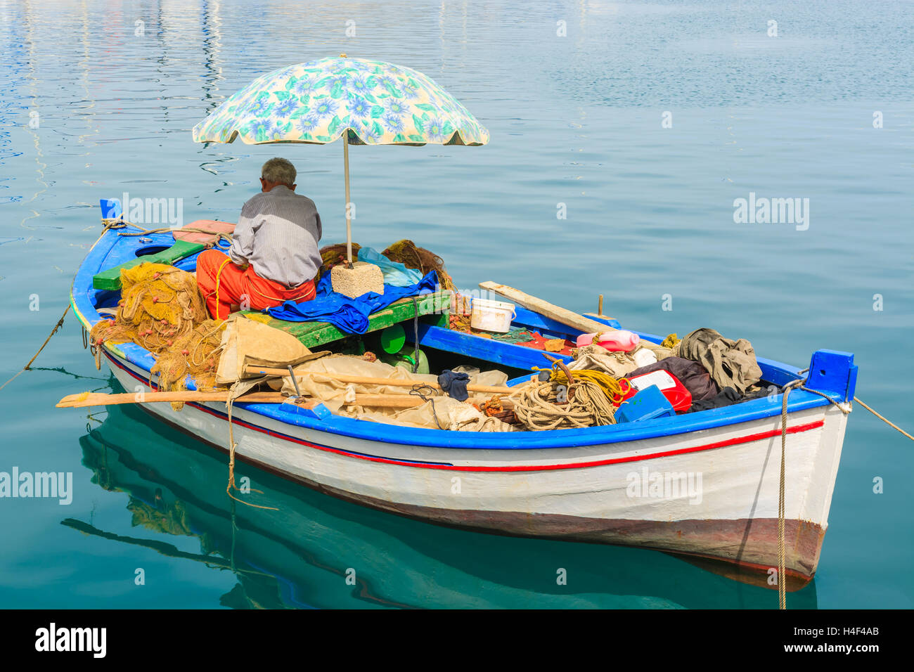 Fisherman sitting on traditional greek fishing boat and cleaning ...