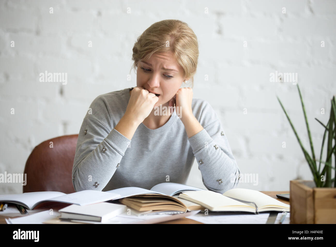 Portrait of a student girl sitting at the desk biting her fist Stock ...
