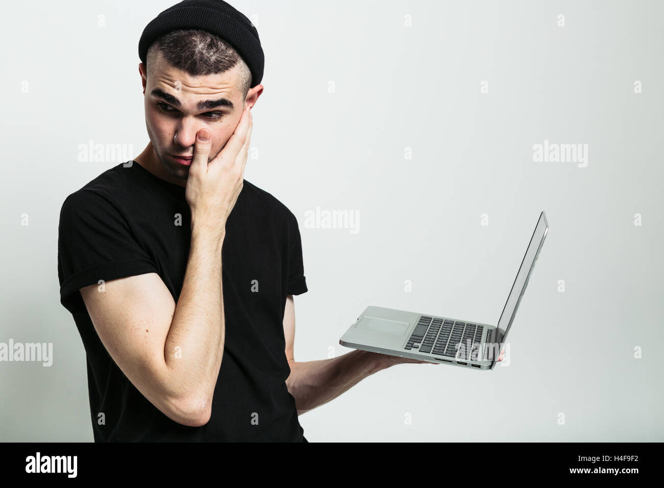 Confused young man with laptop in studio Stock Photo - Alamy
