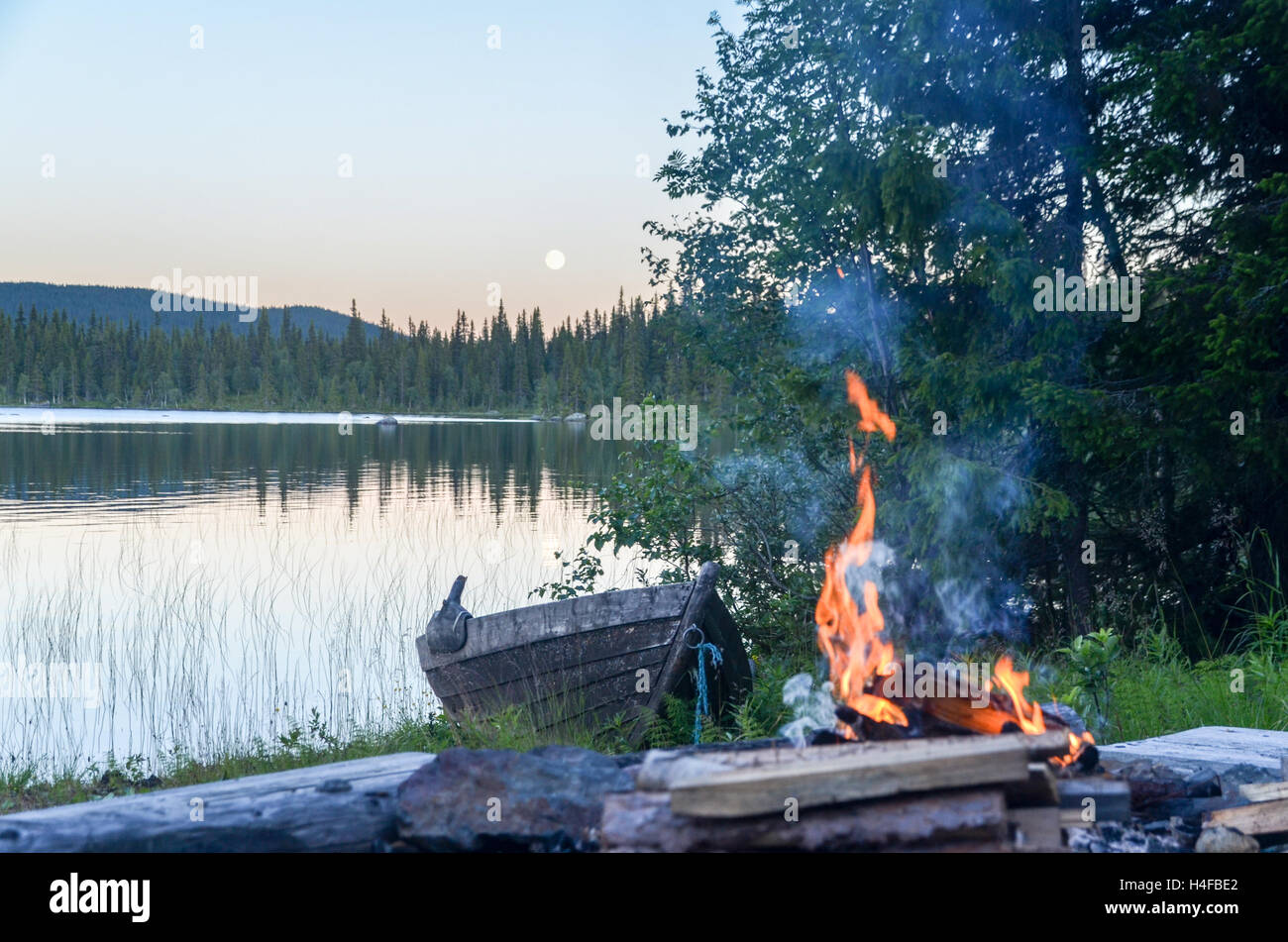 Full moon over a lake in a forest of Sweden, while camping by a fire ...