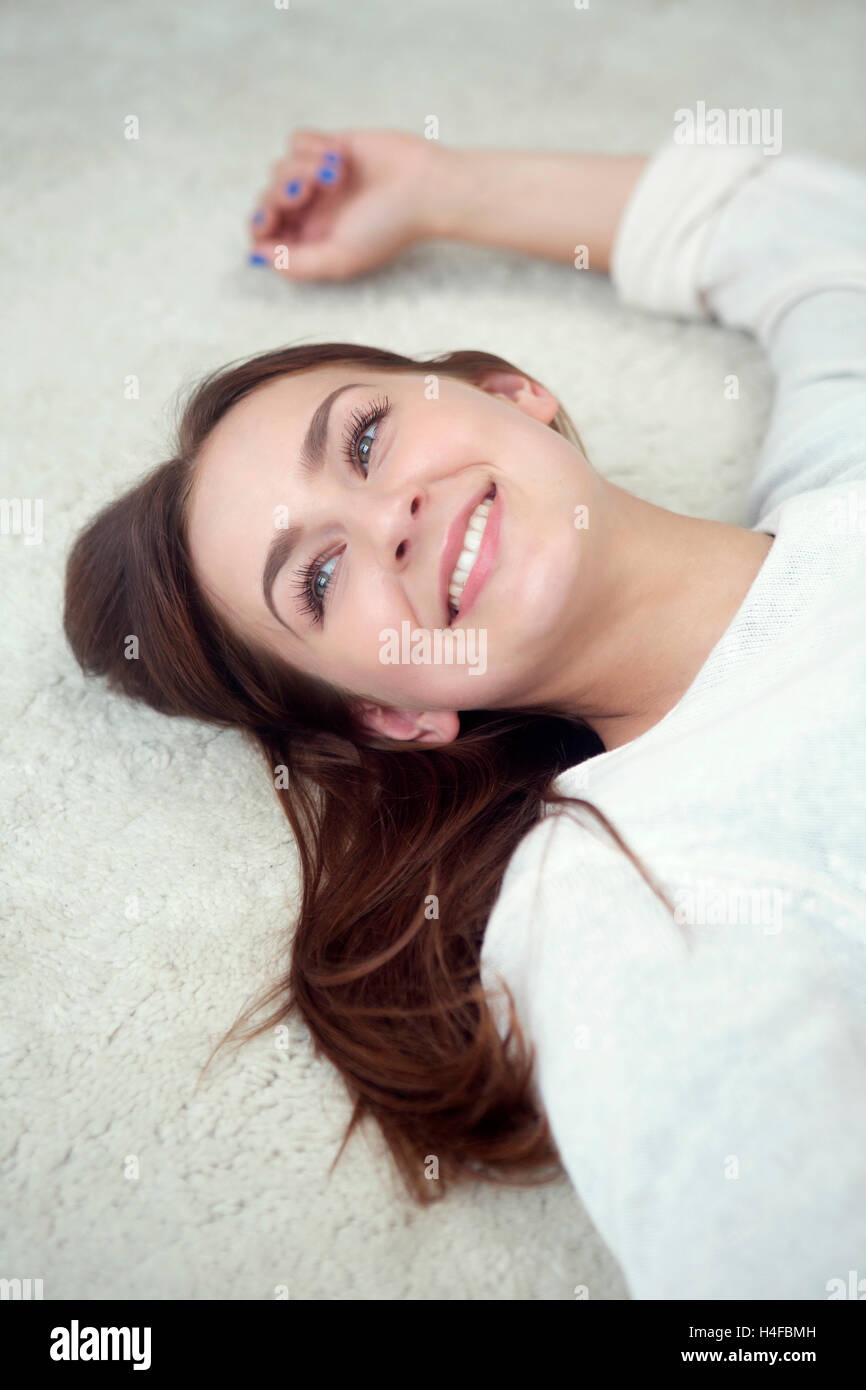 young brunette woman lying on carpet and smiles Stock Photo - Alamy