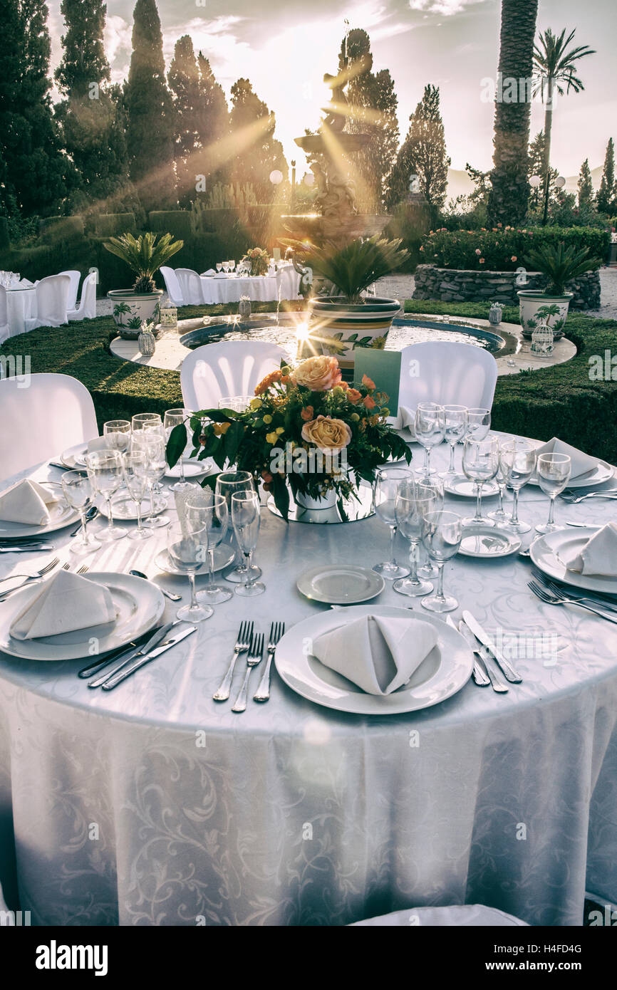 Garden table setting at wedding reception under sunset sun rays ...