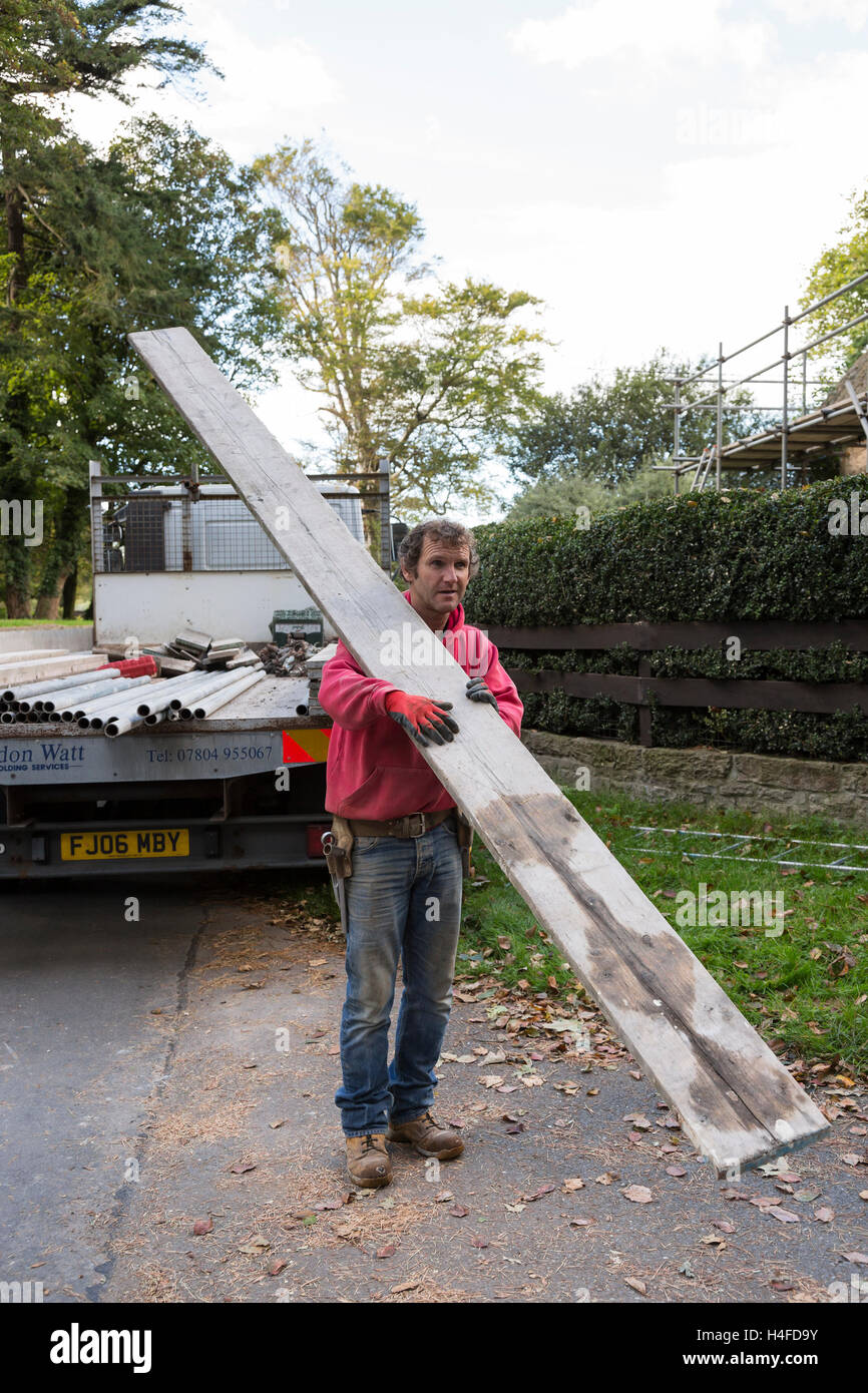 Scaffold worker carrying plank Stock Photo - Alamy