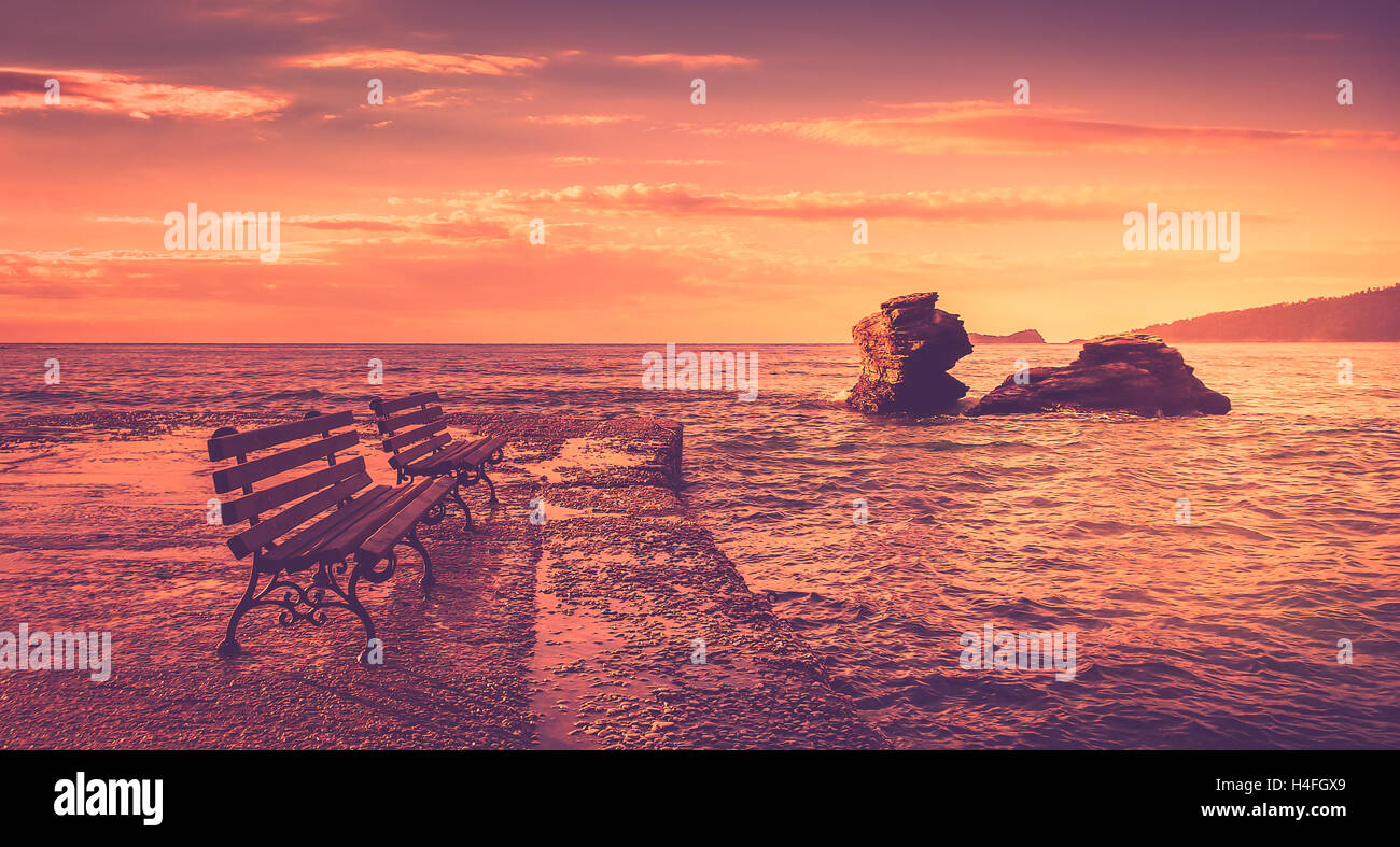 Sunrise scene at the sea. There are two benches and two cliffs into the ...