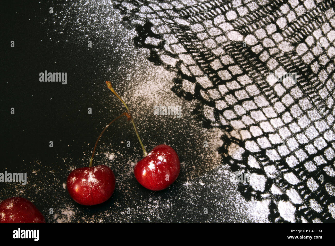 Sweet cherry against black background and lacy drawing from icing sugar ...