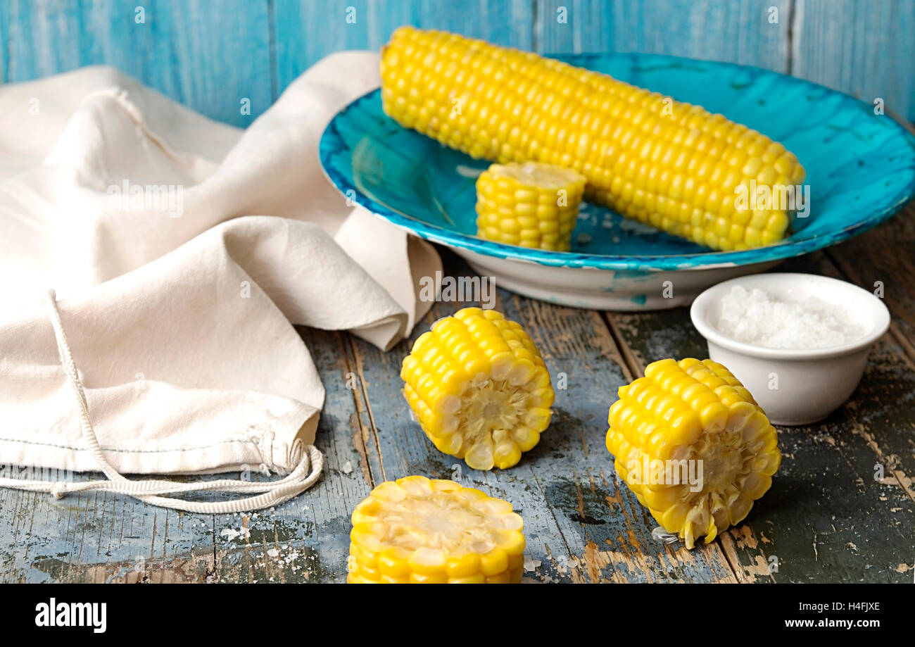 Boiled corn on deep blue plate and chopped ear of corn on old wooden ...