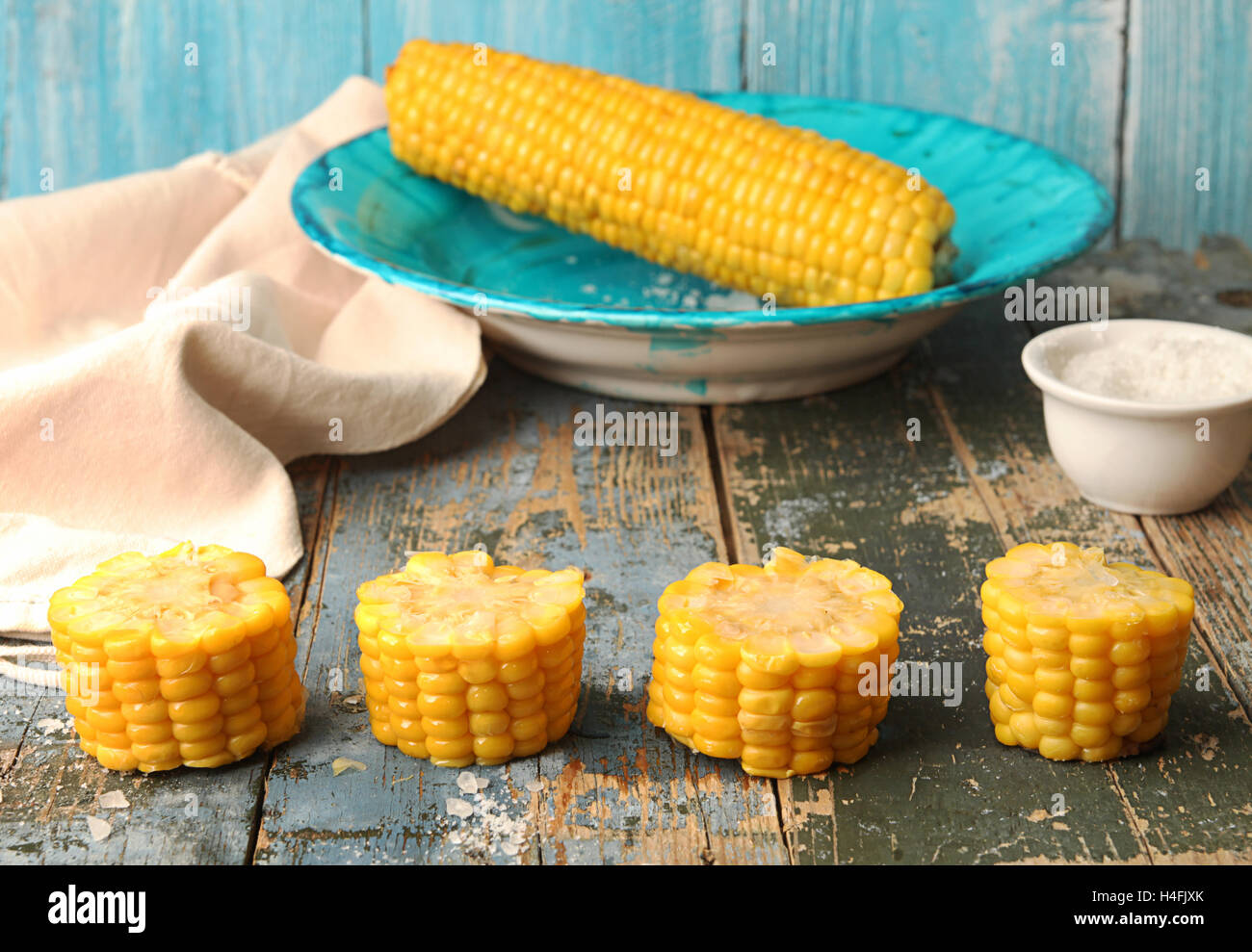 Boiled corn in blue plate and chopped corn ear on rustic wooden table ...