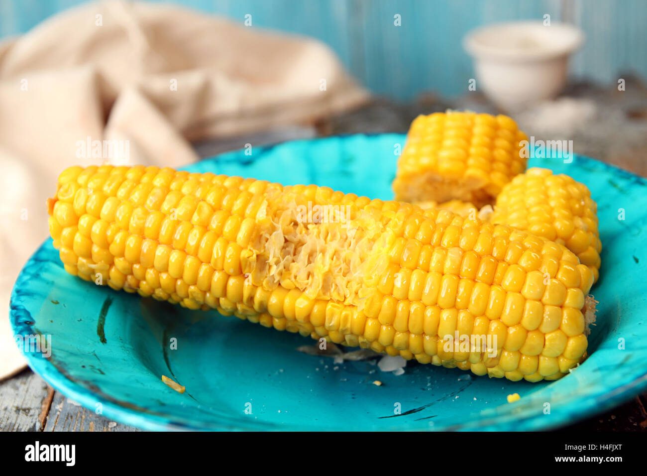 Boiled bitten corn in blue plate and chopped corn ear on rustic wooden ...