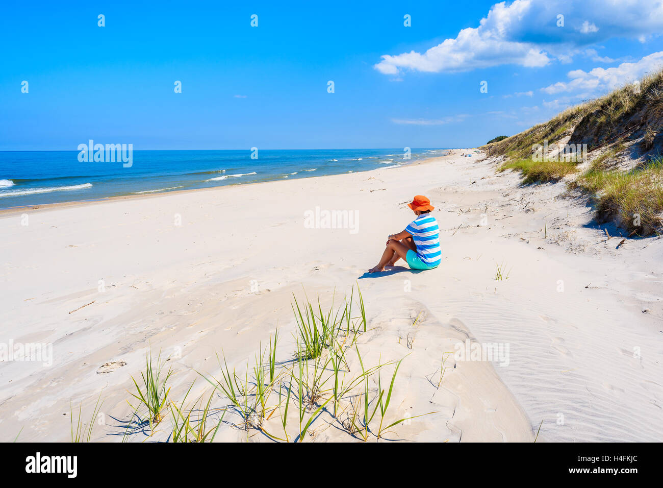 Young woman tourist sitting in sand on beautiful empty beach in Bialogora, Baltic Sea, Poland ...