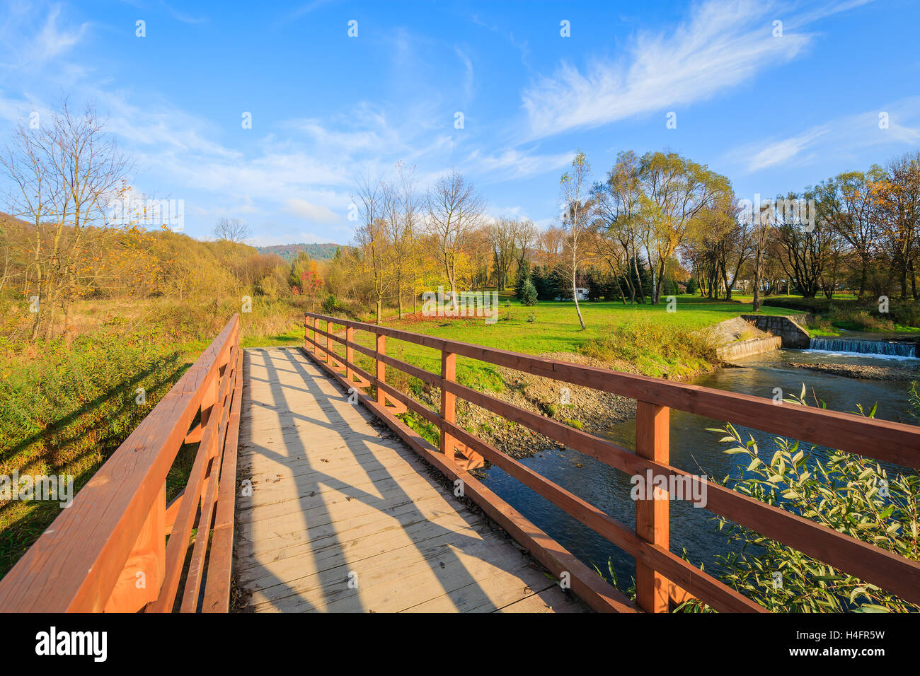 Wooden footbridge over river in a park with colorful trees in autumn ...