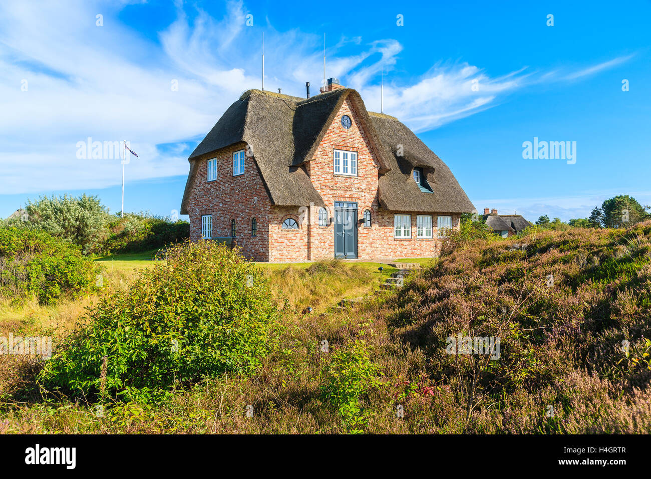 Traditional red brick house with thatched roof on meadow near ...