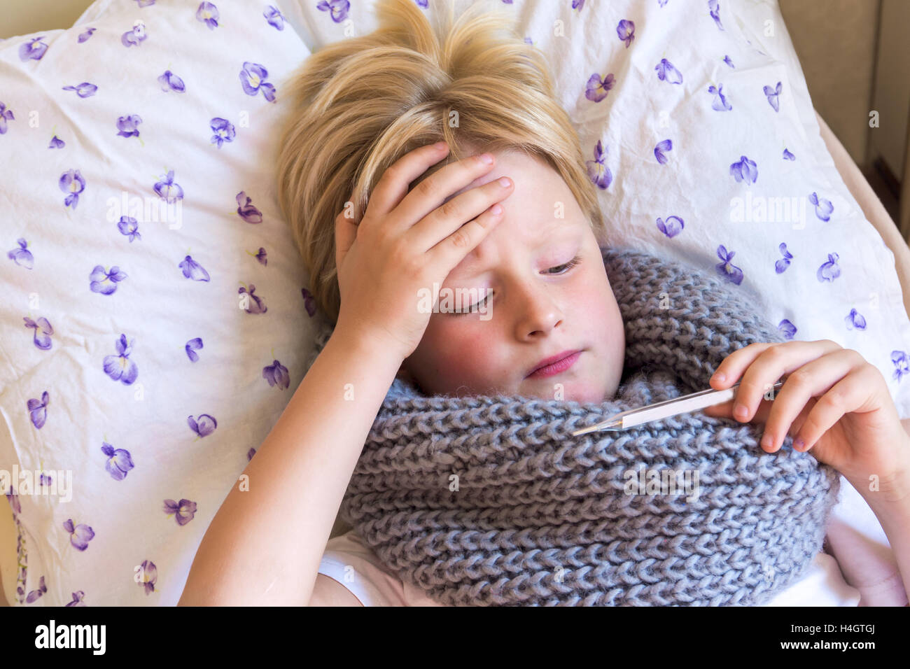 Sick little boy holding thermometer laying in bed with sad face ...
