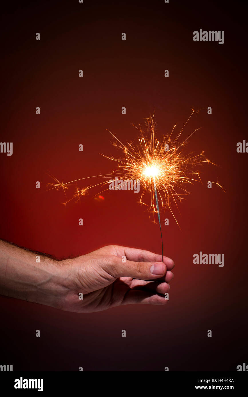 Hand holding sparkler on red background Stock Photo - Alamy
