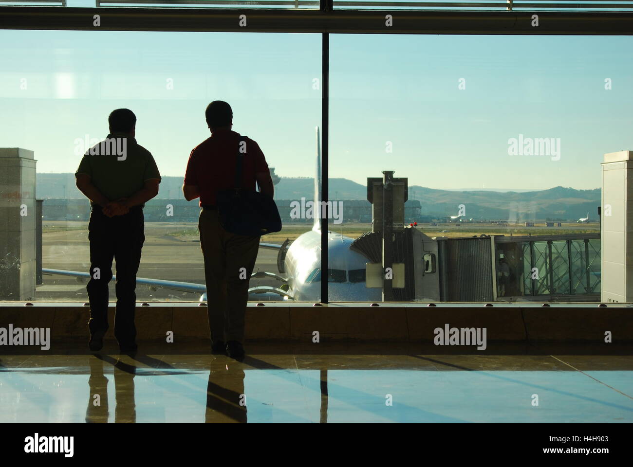 Two men watch an airplane on the tarmac while waiting for their flight ...