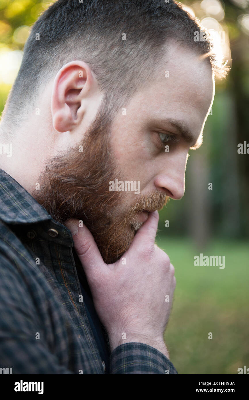 thoughtful young man with a beard is holding his beard with hand Stock ...