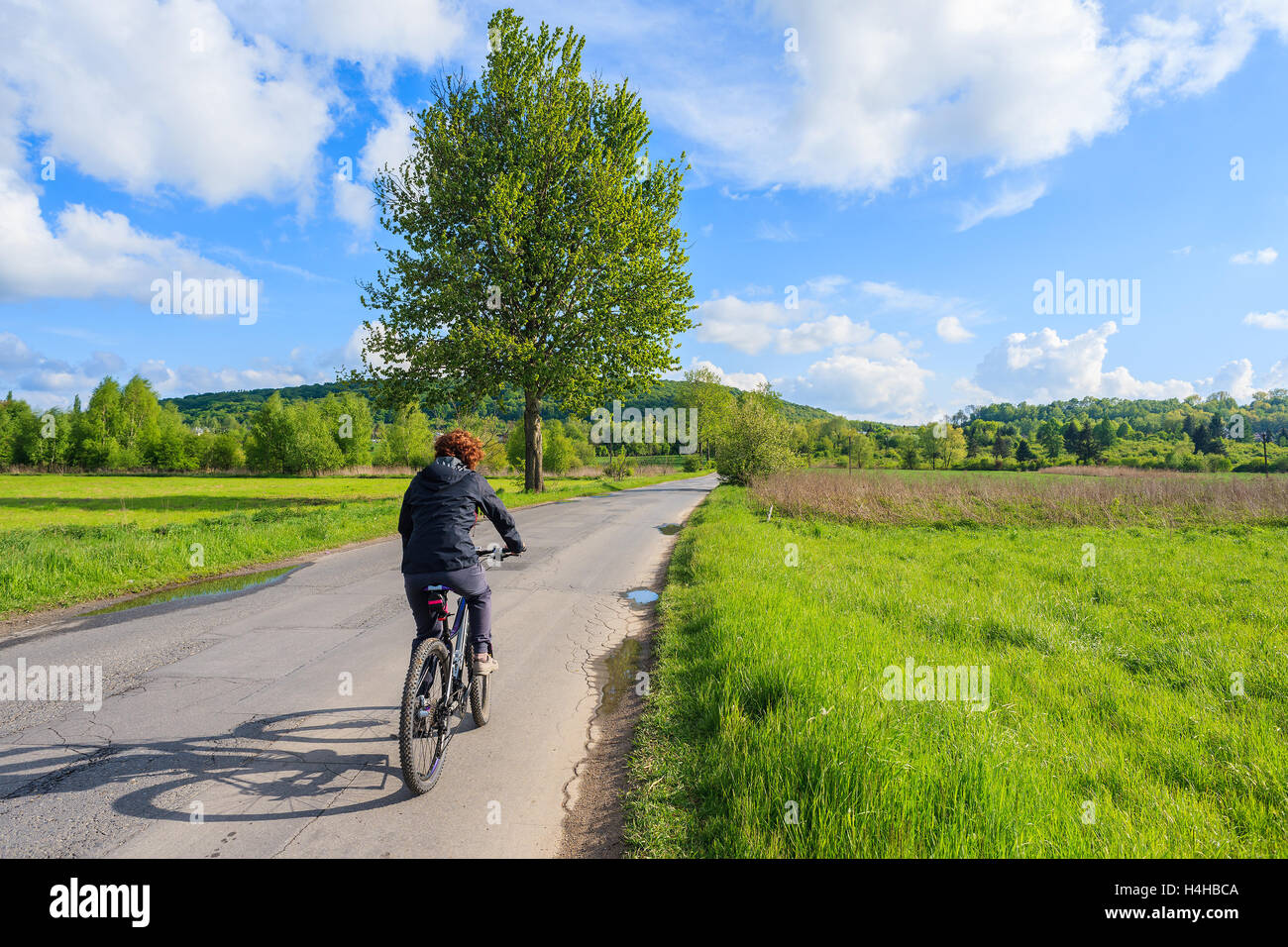 Young woman riding a bike on road along rural landscape near Krakow ...