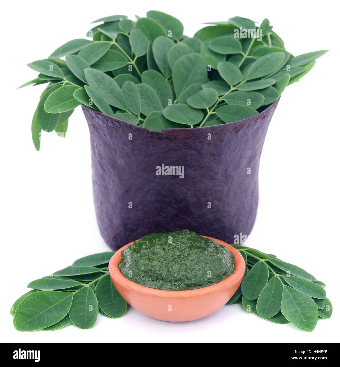 Edible moringa leaves in a vintage mortar with ground paste over white ...