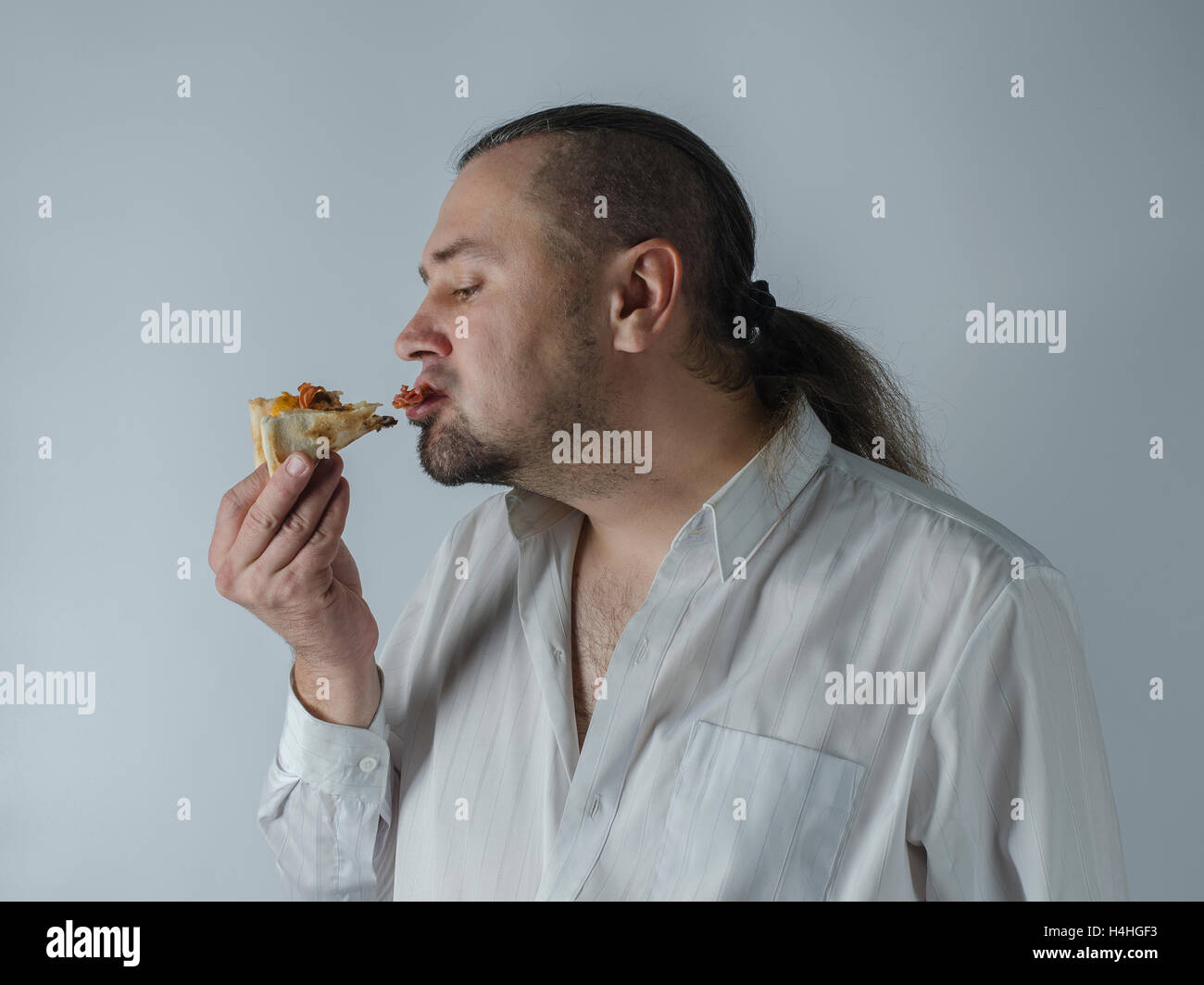 man with long hair in a white shirt eats a slice of pizza Stock Photo ...