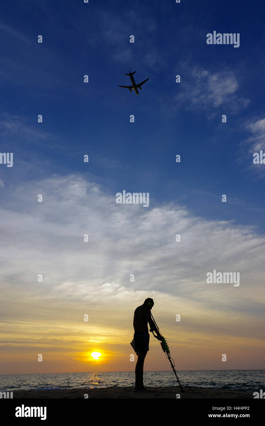 a treasure hunter with Metal detector on sunset on the beach, with a ...