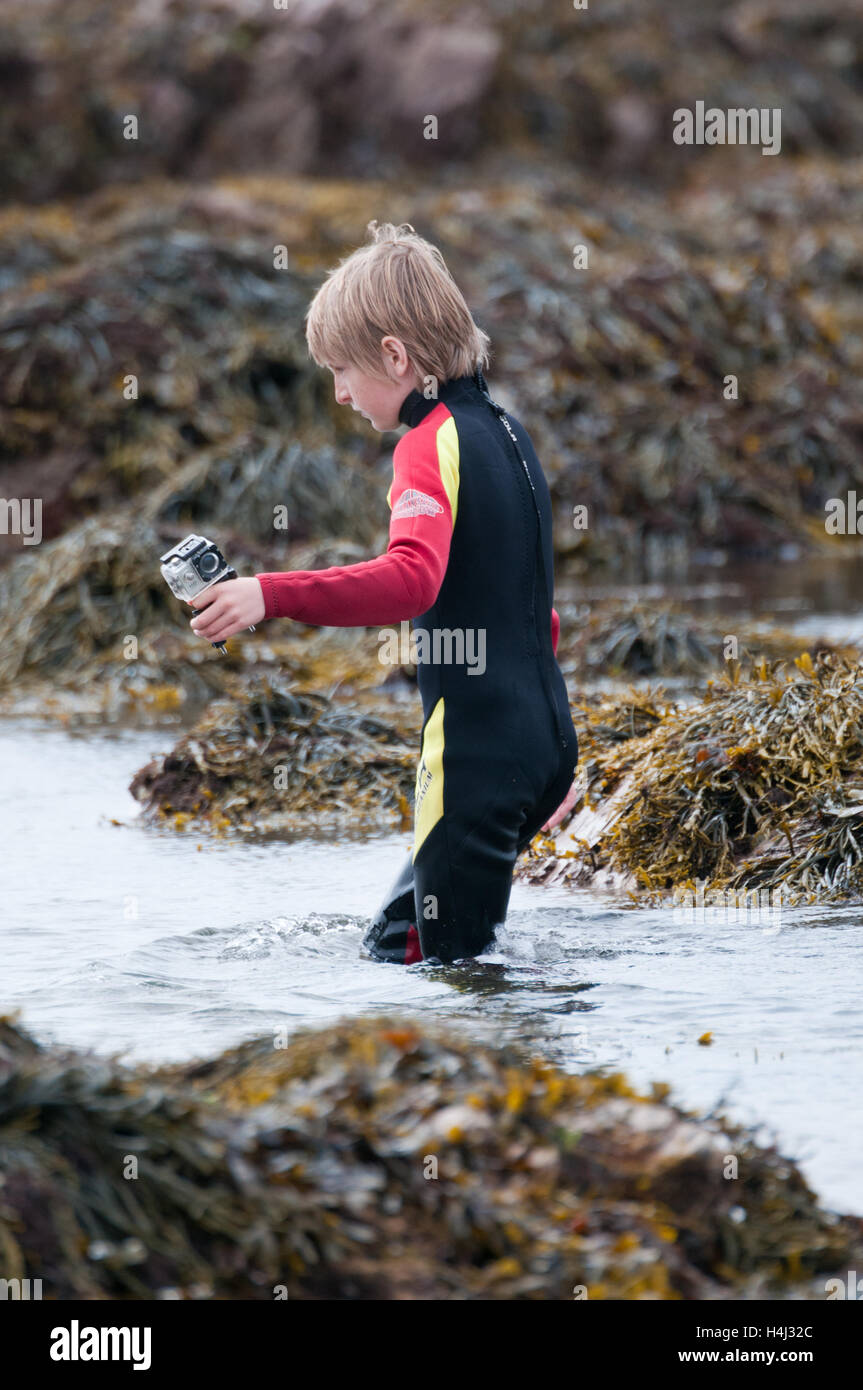 Boy wading through rock pool with action camera Stock Photo - Alamy