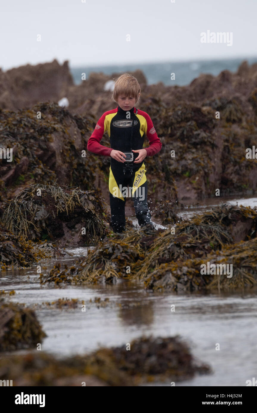 Boy wading through rock pool with action camera Stock Photo - Alamy