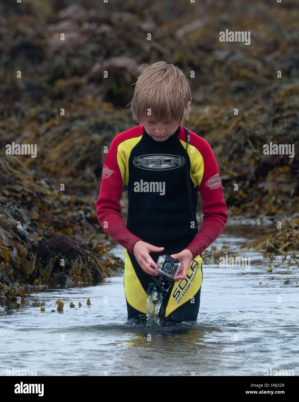Boy wading through rock pool with action camera Stock Photo - Alamy