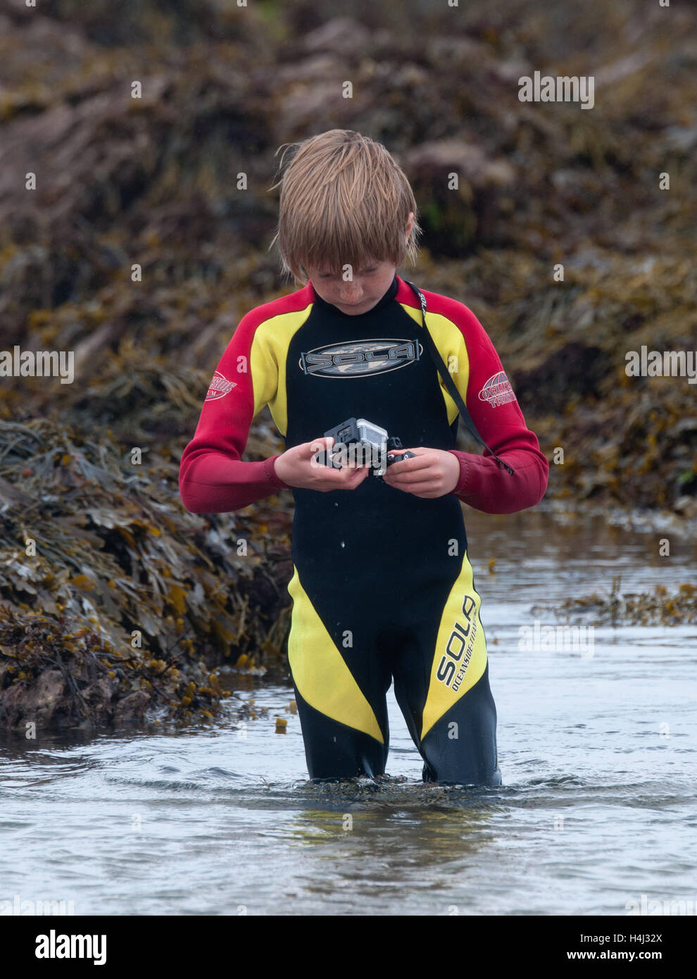 Boy wading through rock pool with action camera Stock Photo - Alamy
