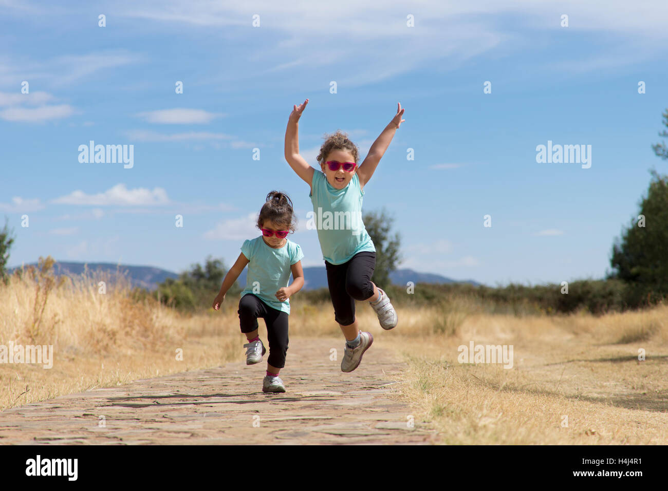 Portrait of little girls in similar wear jumping holding hand in hand ...