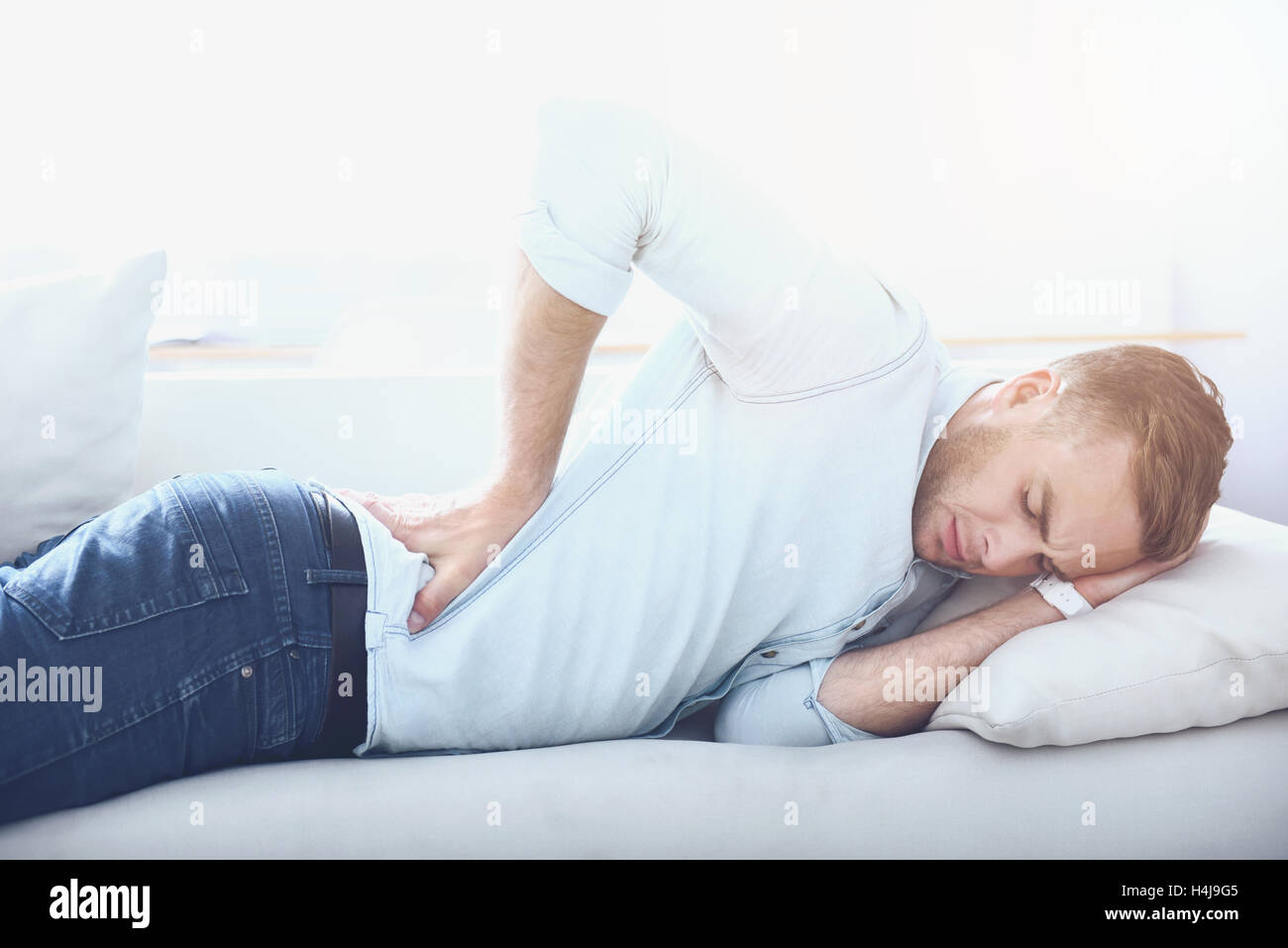 Tired young man laying in the sofa with backache Stock Photo - Alamy