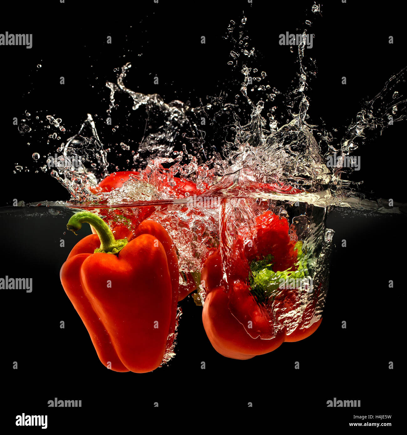 Group of bell pepper falling in water with splash on black background ...