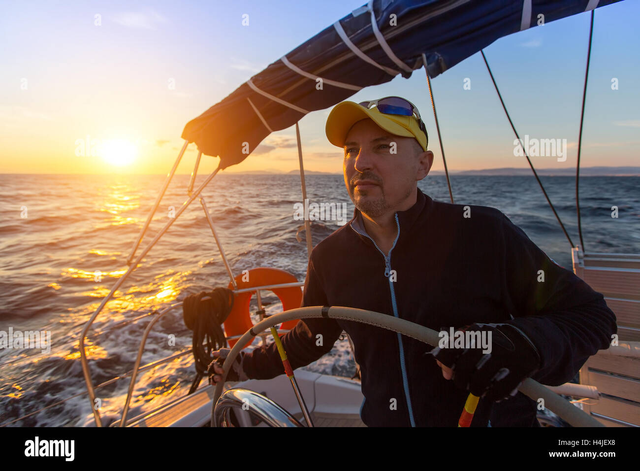 Captain steers the sailing yacht on the sea during sunset Stock Photo ...