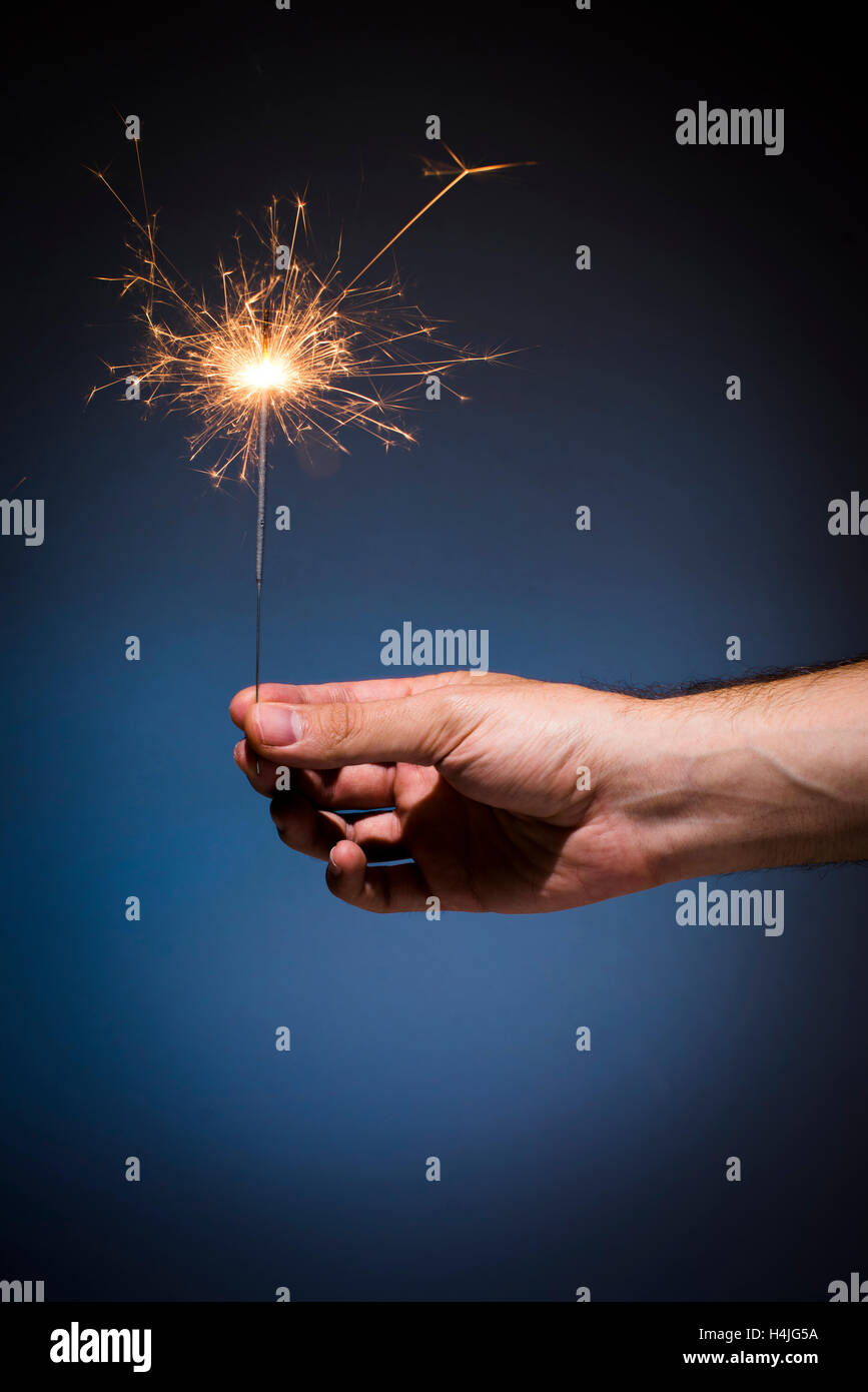 Hand holding sparkler on blue background Stock Photo - Alamy