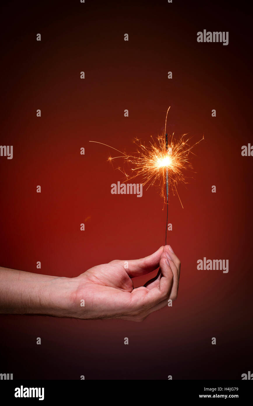 Hand holding sparkler on red background Stock Photo - Alamy