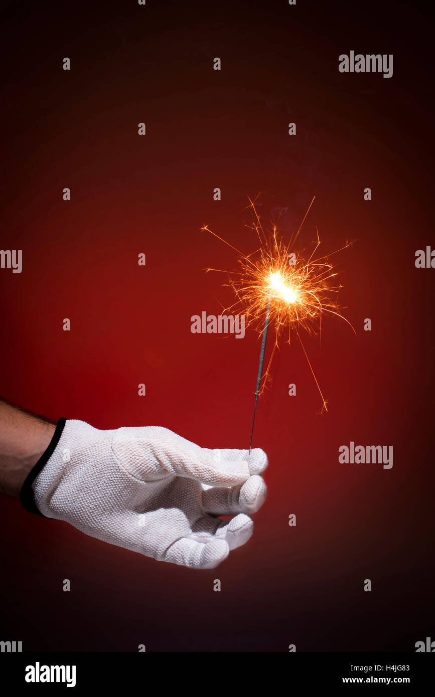 Hand with glove, holding sparkler on red background Stock Photo - Alamy