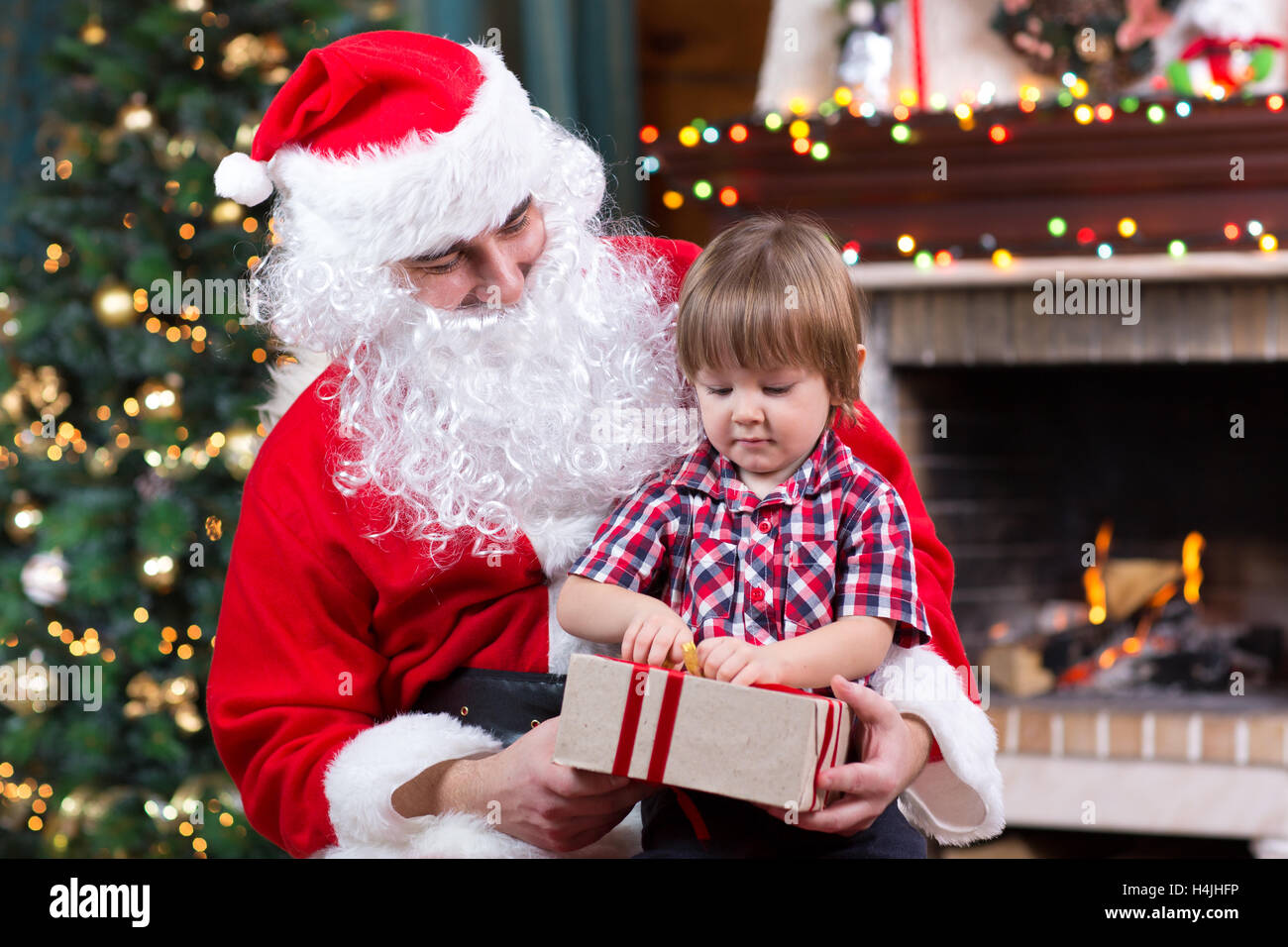 Father weared Santa Claus and kid boy open gift box sitting near by ...