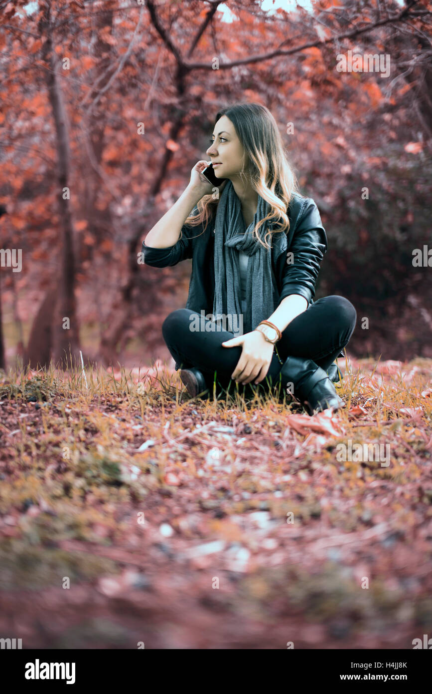 Happy young woman making phone call at woods in autmn. Red leaves ...