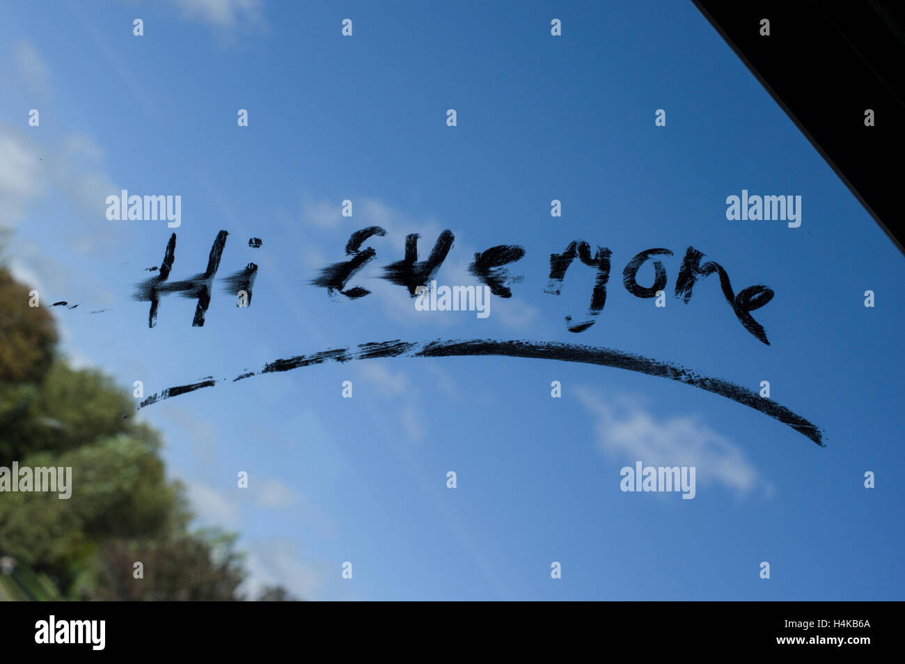 hi everyone scrawled in black marker on a window with blue skies, trees ...