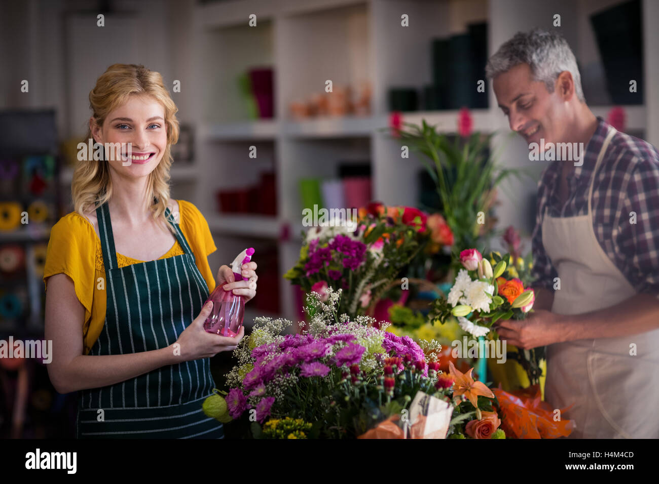 Smiling florist spraying water on flowers in flower shop Stock Photo ...