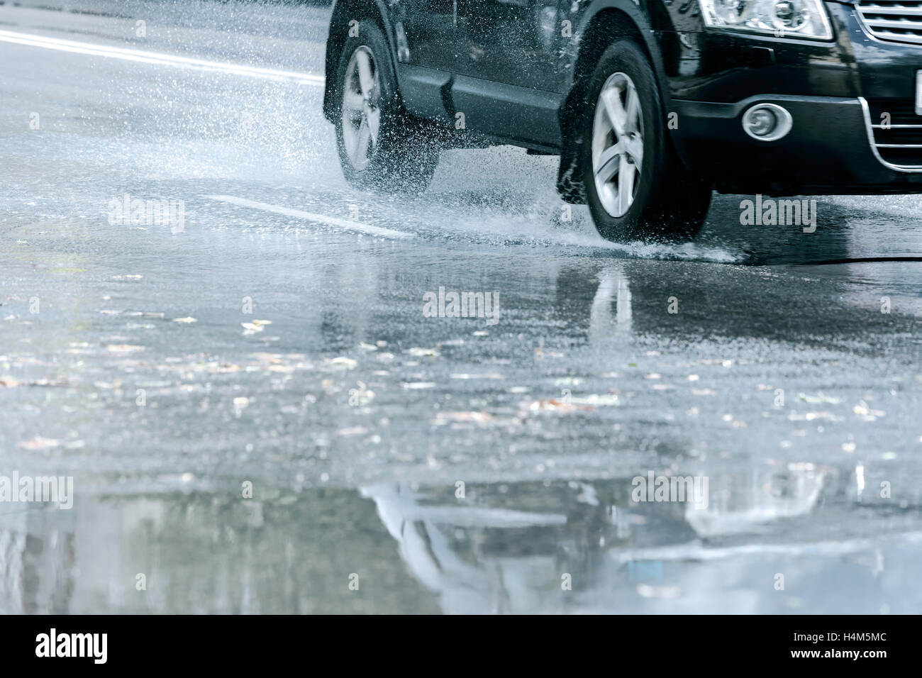 car driving through water puddle and reflecting in it. city road after ...