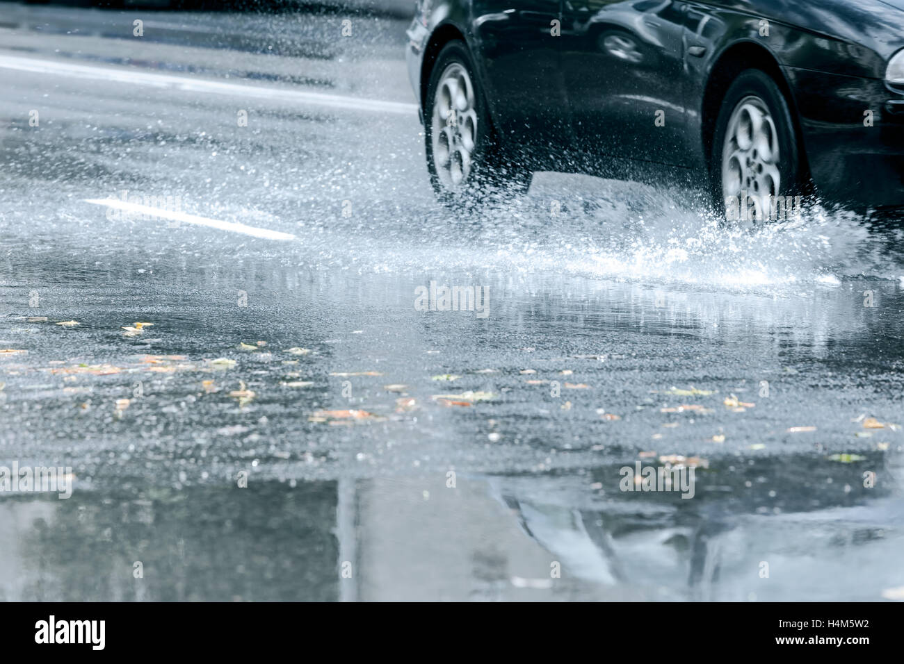 black car driving through rain puddle with splashing water from its ...