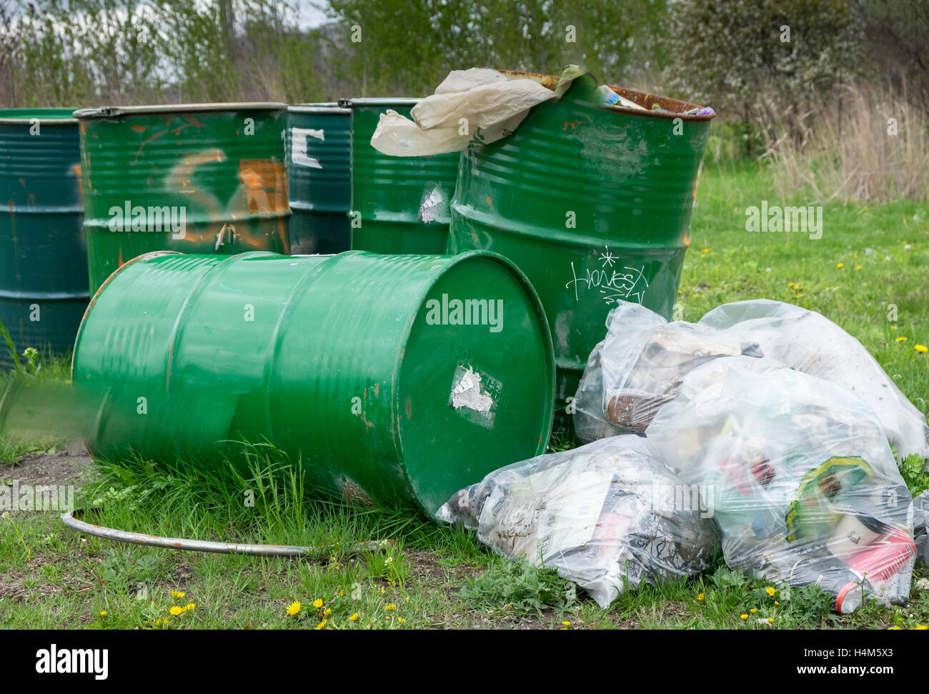 Garbage in plastic bags beside green metal garbage cans in a park in ...