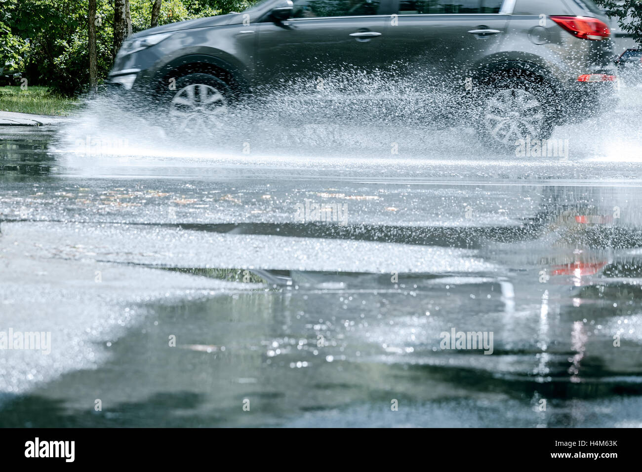 city road after rain. black car driving through rain puddle and ...