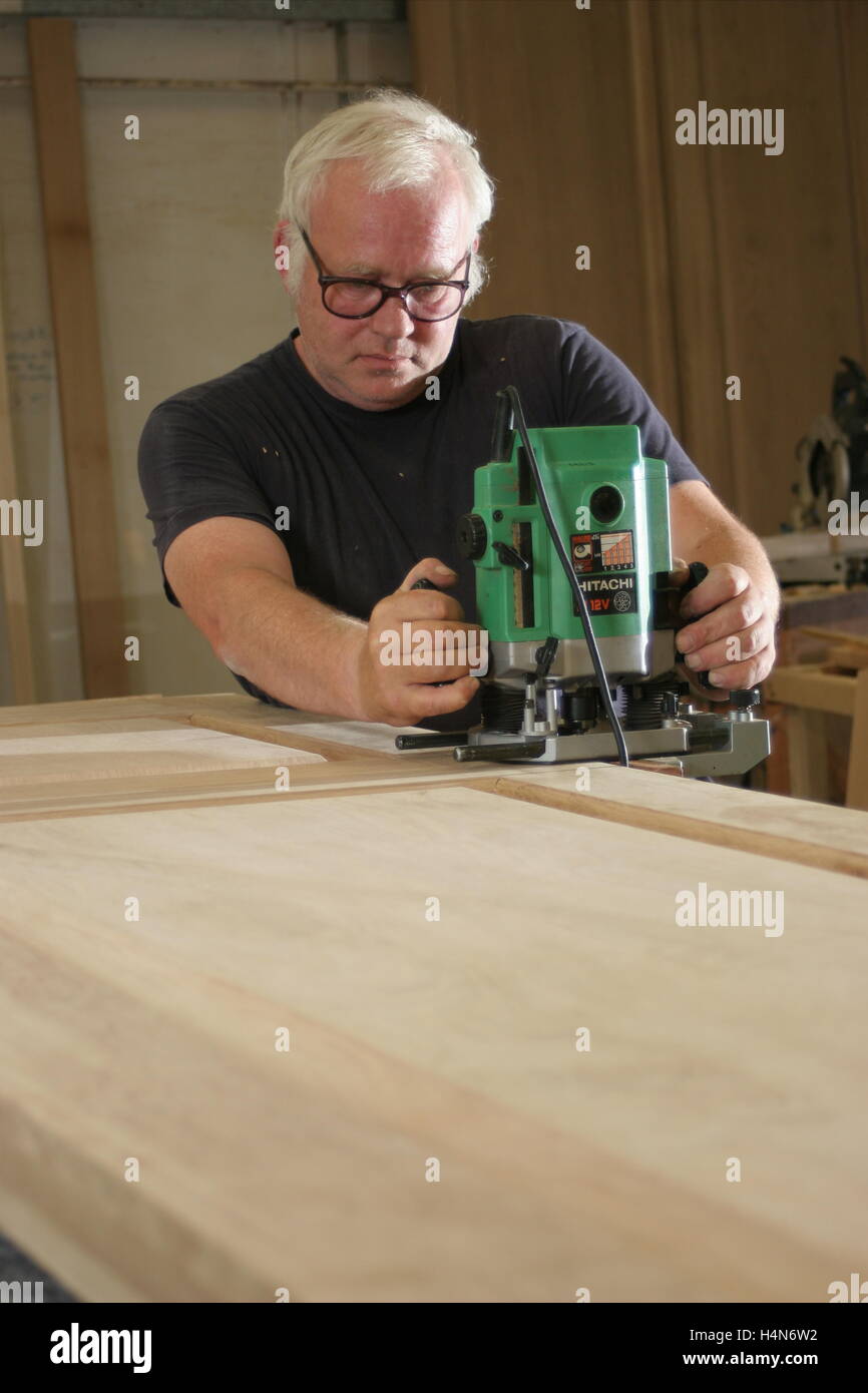 A worker in a joinery workshop uses a routing machine to finish a ...