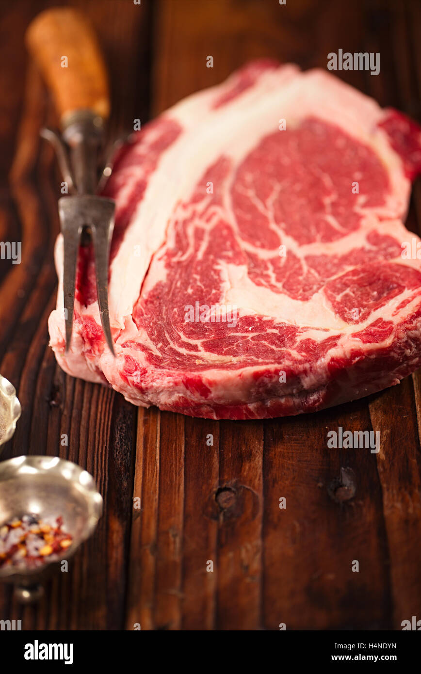 raw beef Ribeye steak on wooden table with vintage carving fork and ...