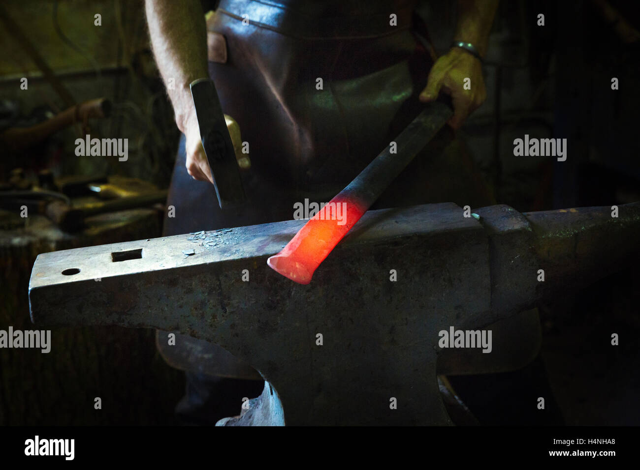 A blacksmith strikes a length of red hot metal on anvil with a hammer ...