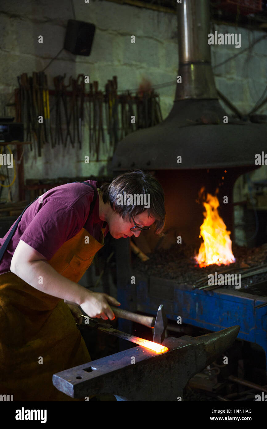 A blacksmith strikes a length of red hot metal on anvil with a hammer ...