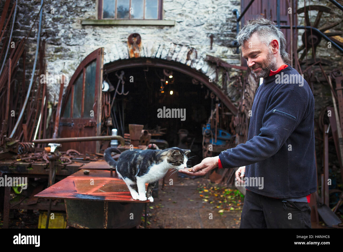 Blacksmith outside his workshop, feeding a cat Stock Photo - Alamy