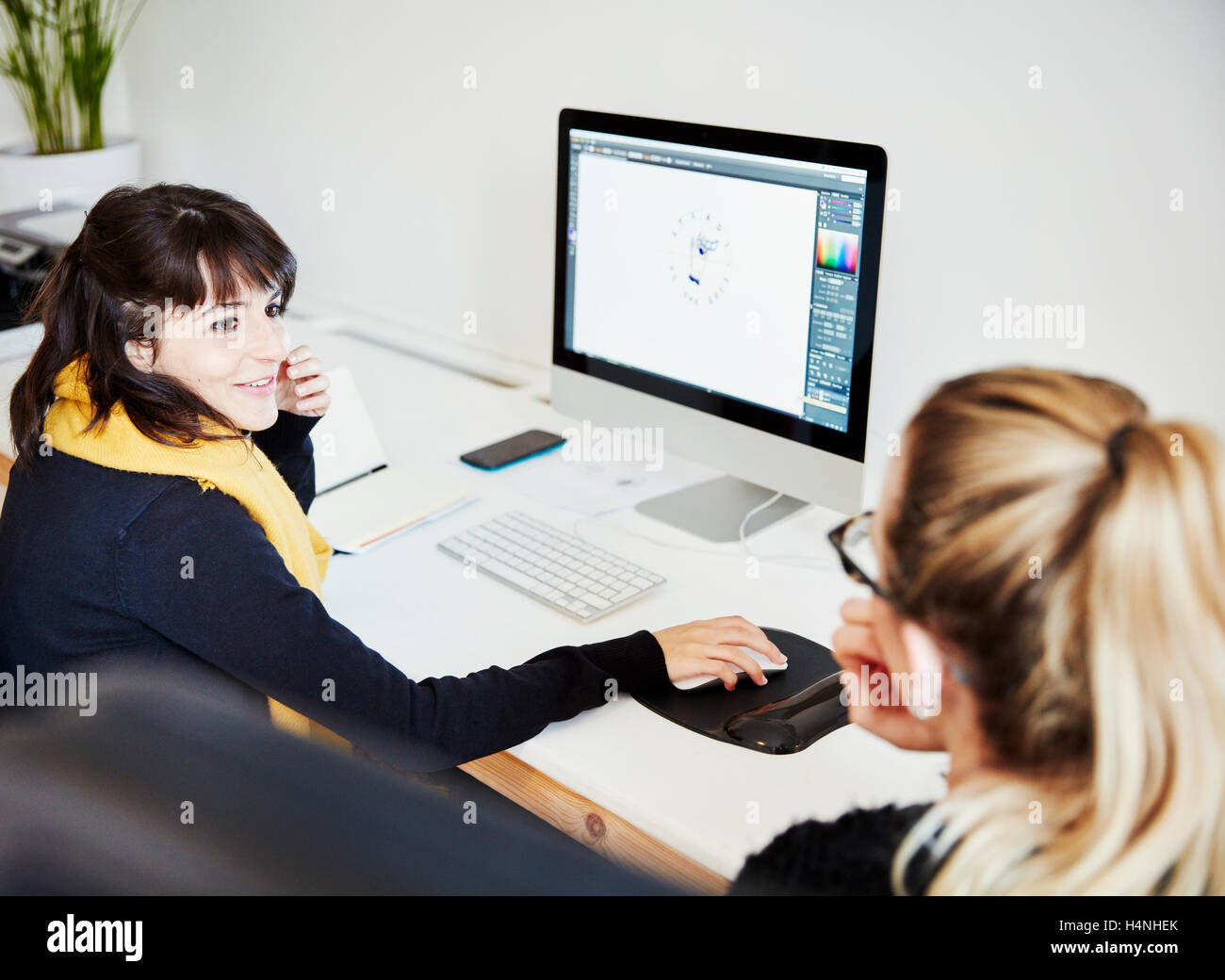 Two women seated sharing a computer screen and discussing the graphic ...