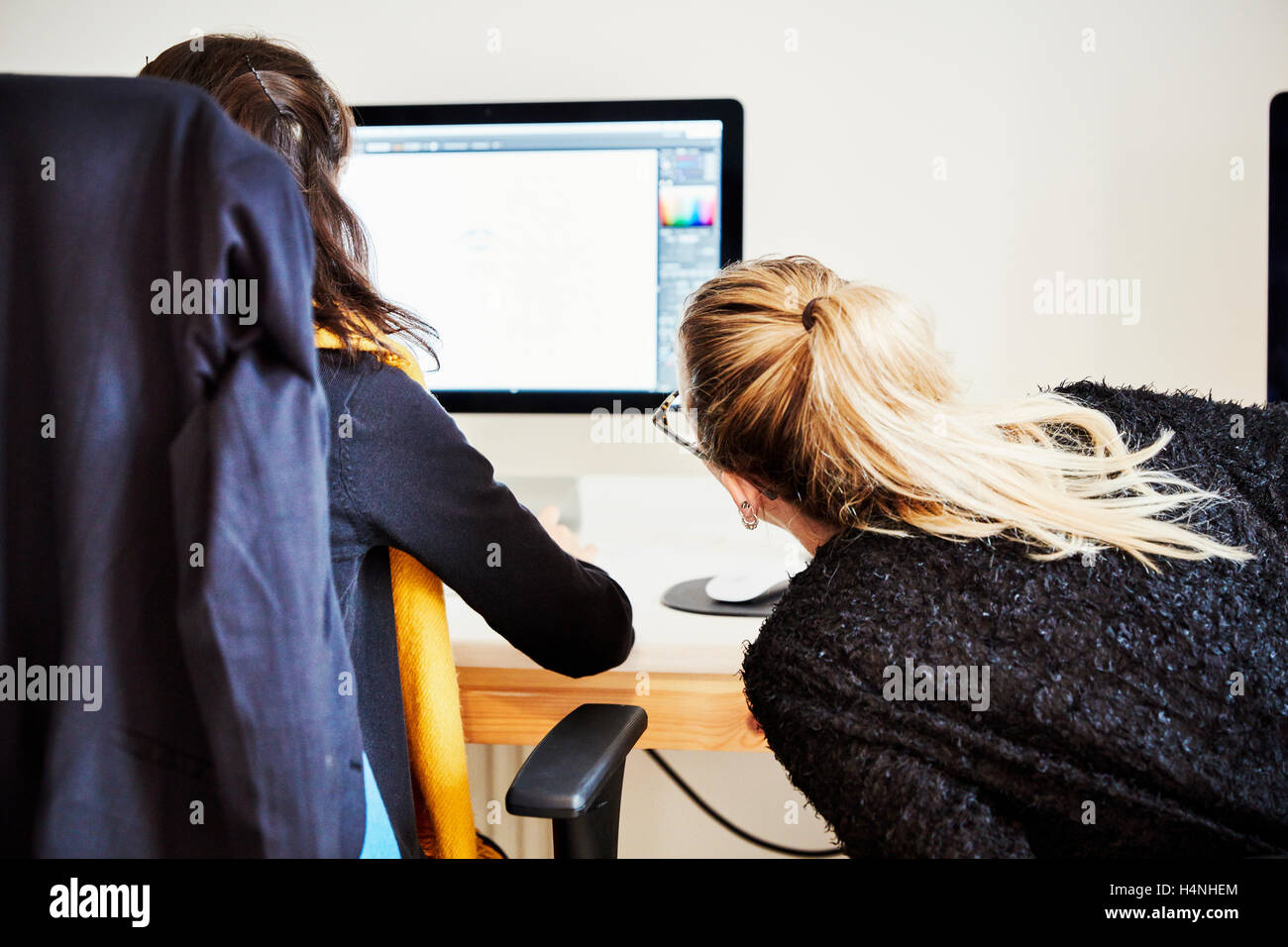 Two women seated sharing a computer screen and discussing the graphic ...