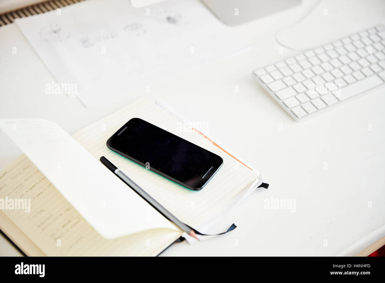 A desk with a computer and white keyboard, paperwork and a smart phone ...
